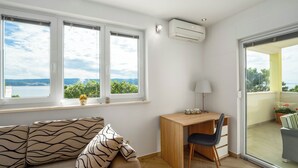 Quarto com escrivaninha, cadeira e sofá, com vista para o exterior.