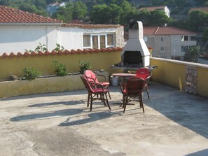 Terraço no telhado com duas cadeiras de vime, uma mesa pequena e uma churrasqueira.