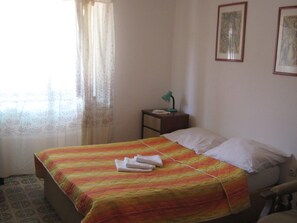 Uma cama bem arrumada com um edredom colorido, uma mesa de cabeceira com abajur e uma cadeira.