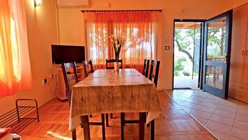 Uma sala de jantar com uma mesa de madeira comprida, cadeiras, uma televisão e uma janela com cortinas laranja.