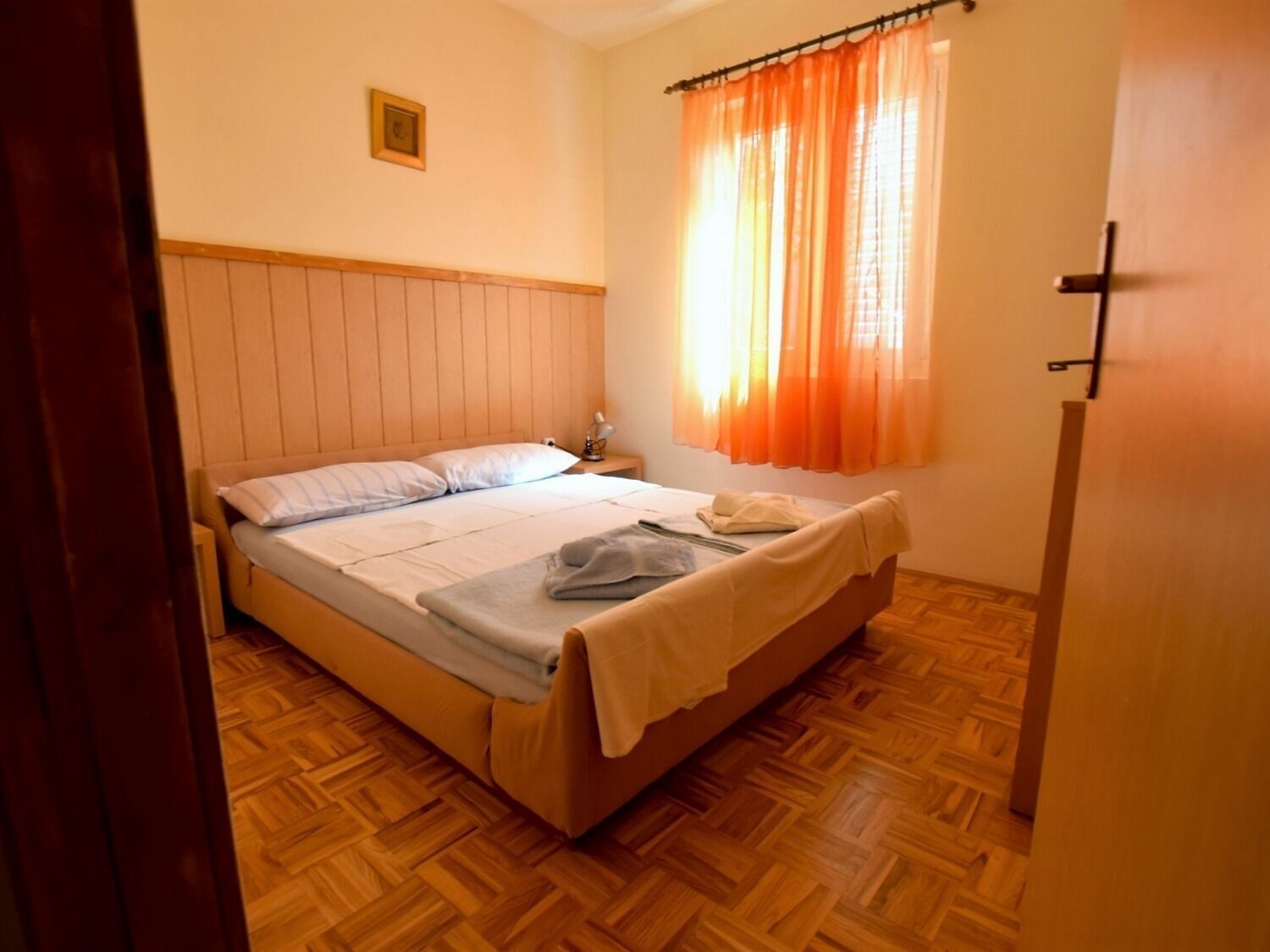 Quarto com cama de madeira, mesa de cabeceira e janela com cortinas laranja.