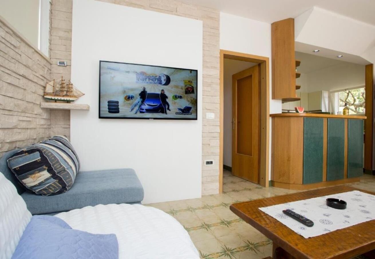 Sala de estar com sofá, mesa de centro com controle remoto e televisão exibindo um anúncio.