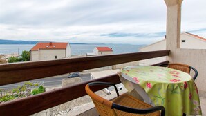 Varanda com cadeiras de vime e uma mesa, com vista para a costa, edifícios e uma estrada.