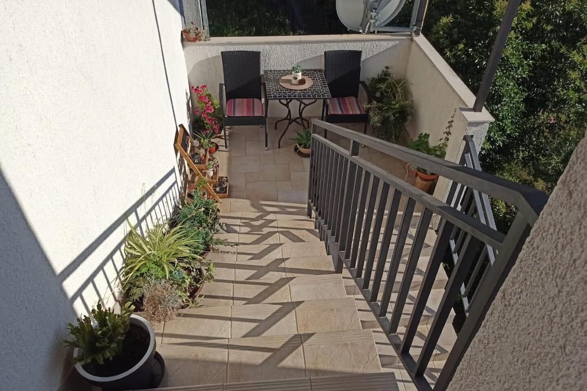 Um espaço ao ar livre iluminado pelo sol, com piso de azulejos, uma mesa pequena com cadeiras e plantas em vasos.