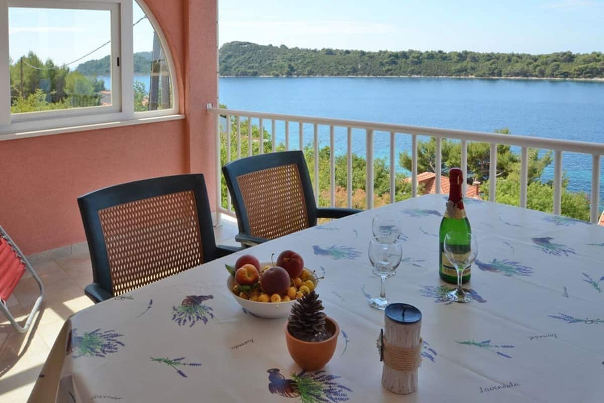 Mesa posta com uma cesta de frutas, taça de vinho e garrafa, com vista para um lago.