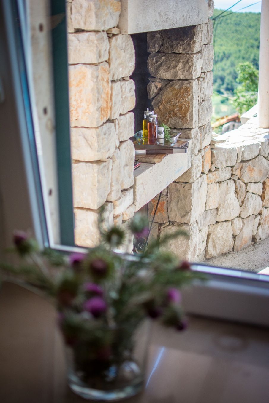 Lareira de pedra com uma prateleira que acomoda garrafas e um vaso com planta.