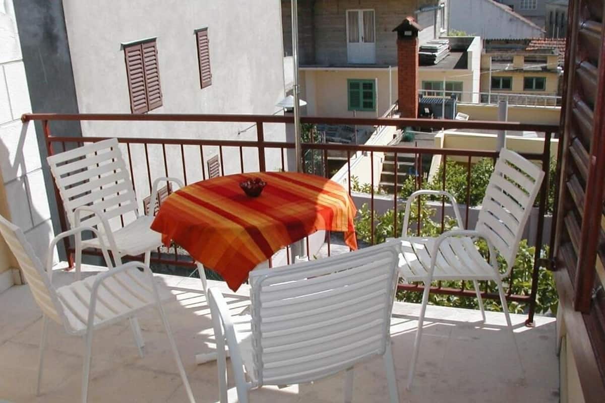 Uma varanda com mesa e cadeiras, vista de edifícios e guarda-corpo.