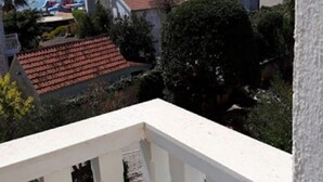 Uma varanda com vista para uma cidade costeira, casas com telhados de barro vermelho e um céu azul límpido.