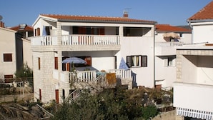 Um edifício residencial de dois andares com varanda, chaminé e um pequeno jardim.