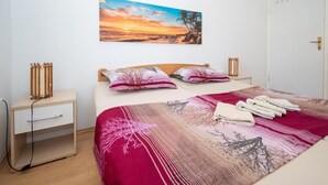 Um quarto com uma cama, mesa de cabeceira, escrivaninha, pintura de um pôr do sol e uma porta.