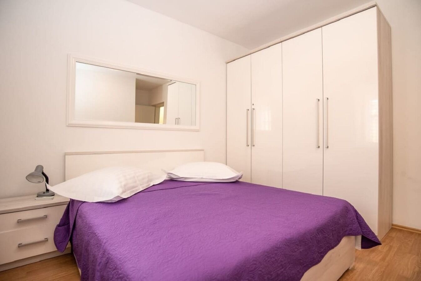 Quarto com cama, mesa de cabeceira, espelho e guarda-roupa.