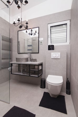 Um banheiro moderno com box de vidro, pia independente, vaso sanitário e lustre.
