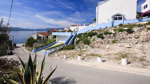 Uma estrada costeira com um edifício branco, com uma escadaria azul e vista para o mar.