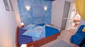 Quarto com cama, luminárias de cabeceira, janela com cortinas e porta que dá para outro cômodo.