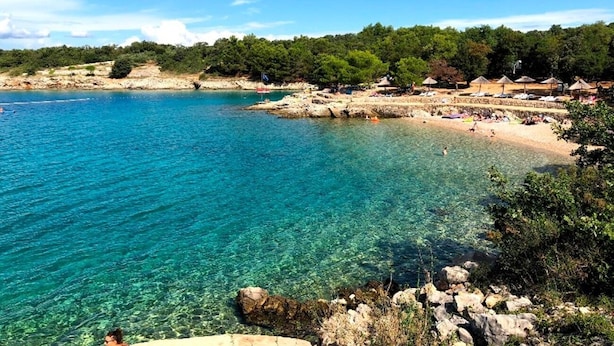 Uma praia costeira com águas turquesa cristalinas, costas rochosas e um cenário com vegetação.