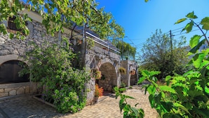 Um edifício de pedra com um pátio pavimentado, uma passagem em arco e cestos com flores penduradas.