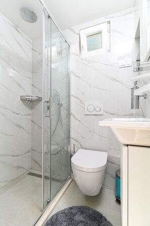 Uma casa de banho moderna com chuveiro separado por vidro, sanita branca e lavatório com espelho em cima.
