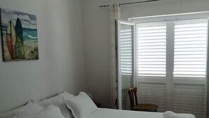 Quarto com cama, almofadas, pintura de pranchas de surf, cadeira e janela com persianas.