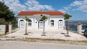 Um edifício de dois andares com telhado de telhas vermelhas, paredes brancas e entrada com piso de pedra.