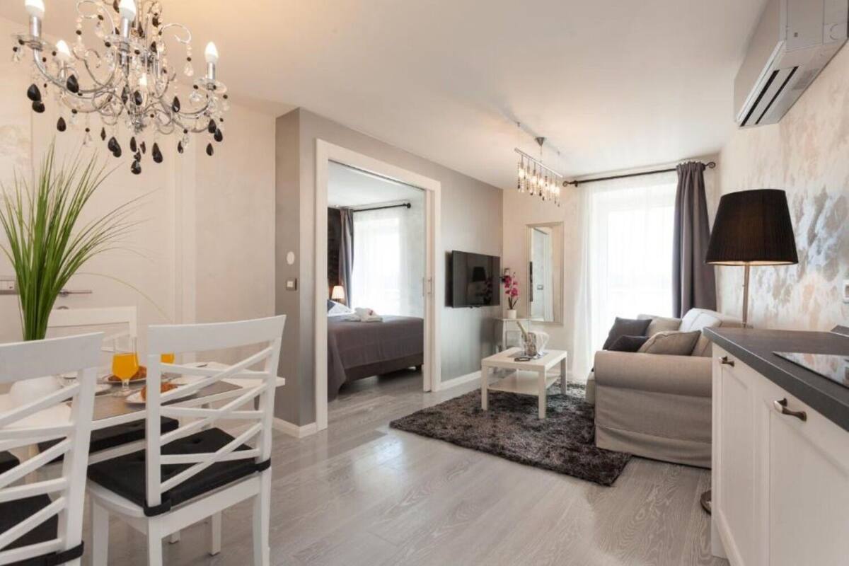 Quarto de hotel moderno com área de refeições, sala de estar, um espelho grande e um candelabro.