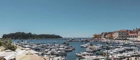 Uma marina com vários barcos atracados, uma pequena ilha ao fundo e uma cidade costeira com edifícios.