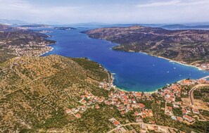 Vista aérea de uma cidade costeira com um porto de recreio, rodeada por colinas e uma grande extensão de água.