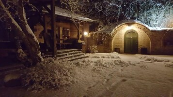 Pátio coberto de neve com um edifício de tijolo, apresentando uma entrada em arco e degraus que levam a um alpendre.