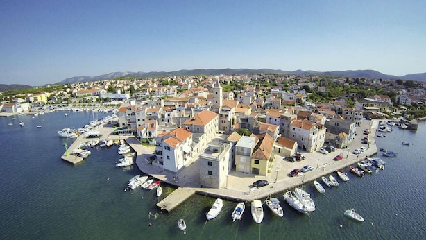 Uma cidade costeira com um porto cheio de barcos, rodeada por edifícios residenciais e colinas ao fundo.