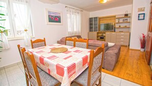 Uma sala de jantar com mesa posta para quatro pessoas, um sofá e uma cozinha com armários e televisão.