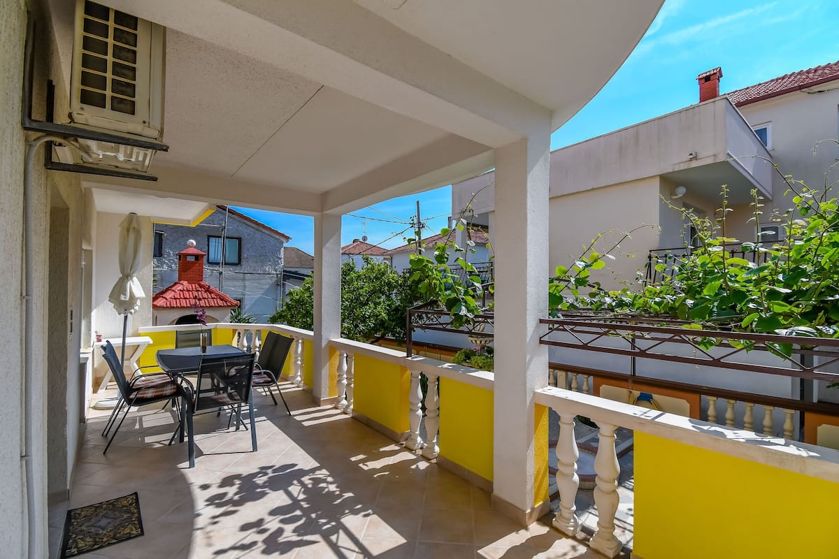 Uma área externa coberta com mesa e cadeiras, um guarda-sol vermelho e um corrimão amarelo.