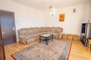 Uma sala de estar com sofá seccional, mesa de centro, tapete e televisão.
