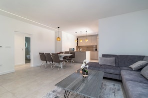Uma sala de estar moderna com mesa de centro de vidro, sofá cinza e área de jantar com cadeiras.