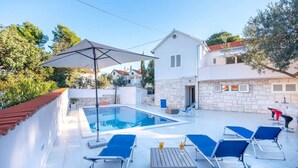 Piscina com espreguiçadeiras e área coberta, cercada por paredes de pedra e um edifício branco.