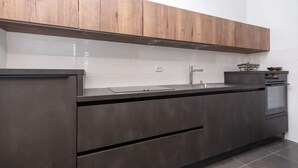 Cozinha moderna com armários escuros, cuba de aço inoxidável e forno embutido.