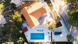 Vista aérea de uma propriedade residencial com piscina, varanda coberta e um edifício com telhado vermelho.