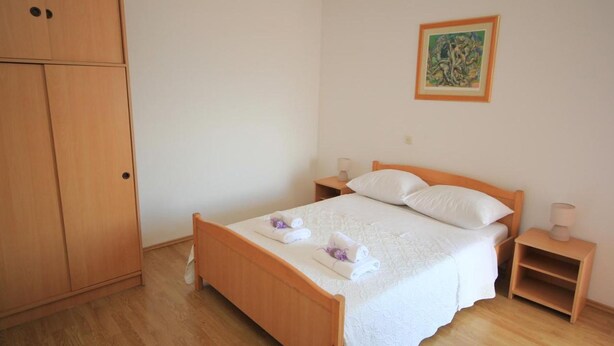 Quarto com cama de madeira, duas mesas de cabeceira, guarda-roupa e um quadro na parede.