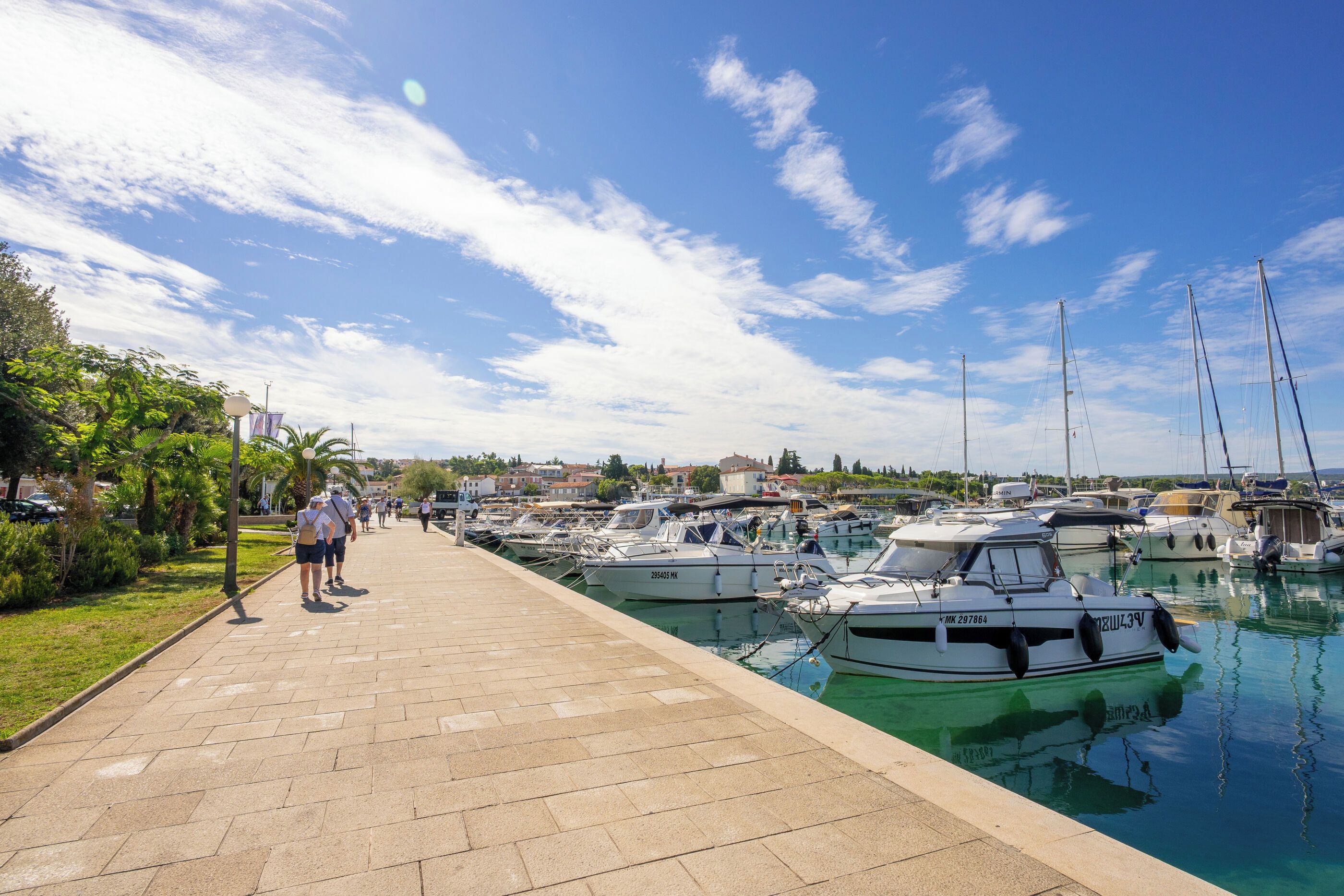 Marina com barcos atracados, calçada pavimentada e céu claro.
