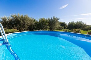 Piscina azul clara com uma escada do lado esquerdo, rodeada por vegetação exuberante e árvores.