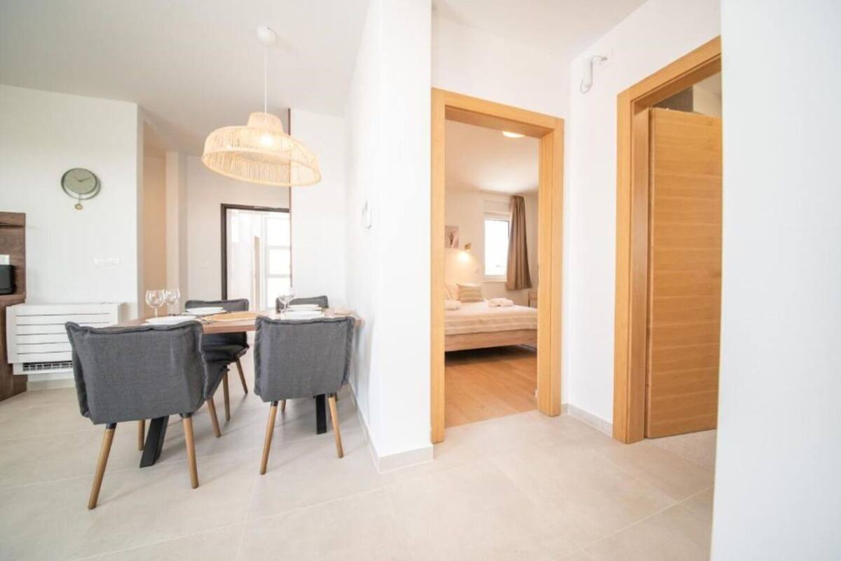 Um interior moderno com área de refeições, incluindo uma mesa, cadeiras, luminária pendente e uma cama visível no quarto adjacente.
