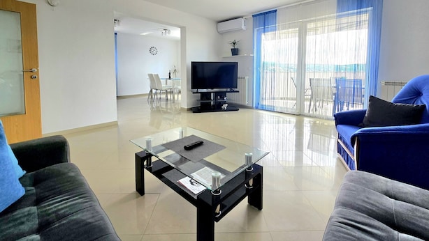 Uma sala de estar moderna com uma mesa de centro de vidro, um sofá, uma TV e um espaço de jantar com cadeiras e uma mesa.