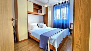 Quarto com cama, guarda-roupa de madeira e janela com cortinas azuis.
