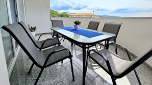 Varanda com mesa e cadeiras, um vaso de planta e vista para edifícios e montanhas.