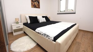 Um quarto com uma cama, mesa de cabeceira, abajur, janela e um quadro na parede.