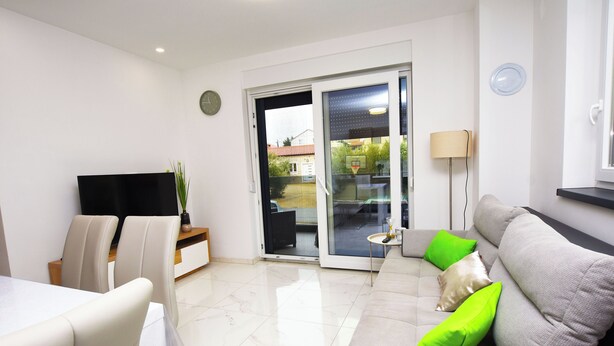 Uma sala de estar moderna com sofá, cadeiras, televisão e uma porta de vidro deslizante que dá para uma área externa.