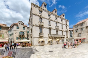 Um edifício histórico com vários andares, janelas amplas e uma estátua em frente.