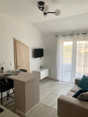 Uma sala de estar moderna com sofá, área de jantar com mesa e cadeiras, TV na parede e varanda com cortinas.