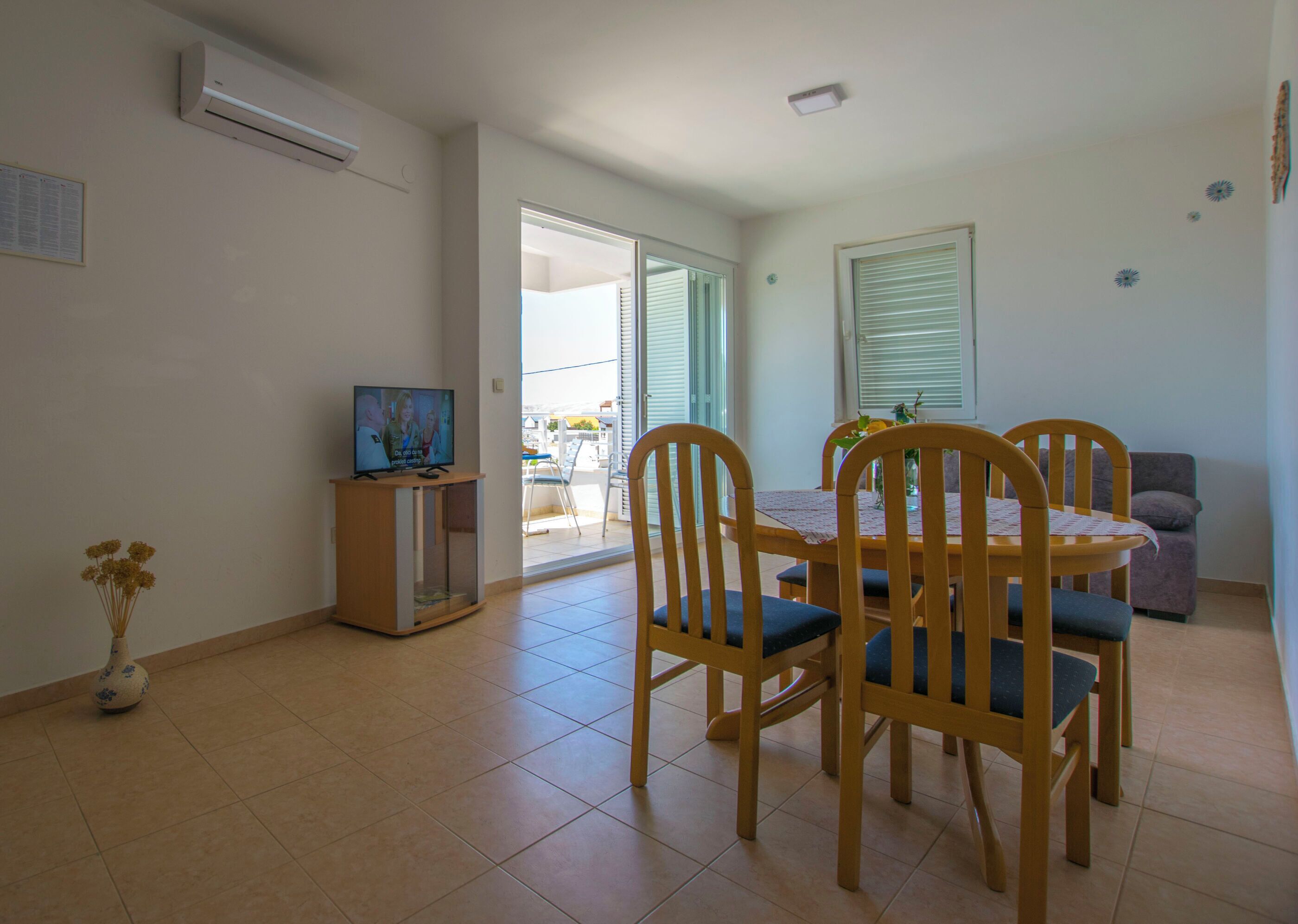 Uma sala de jantar com televisão em um suporte, mesa com cadeiras e um sofá.