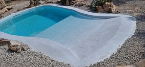 Piscina retangular com borda branca, rodeada por pedras e rochas.