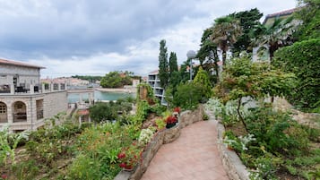 Um caminho de jardim leva a um edifício de pedra, com vista para um corpo d'água e vegetação ao redor.