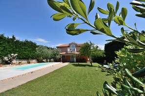 Uma casa com piscina, gramado bem cuidado e jardim.